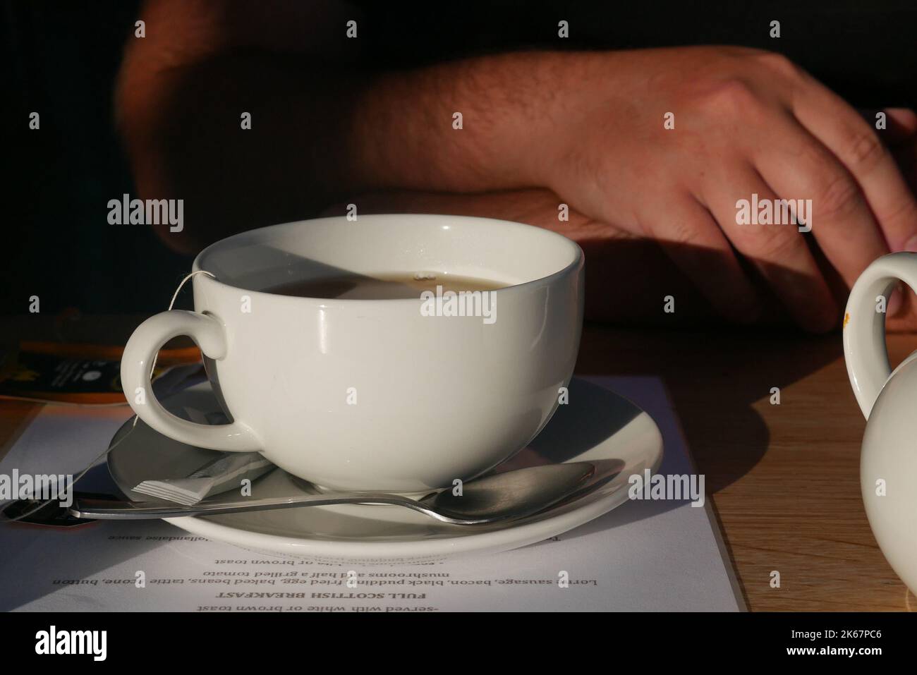 A plain white tea cup on a saucer with spoon sits on a table ...