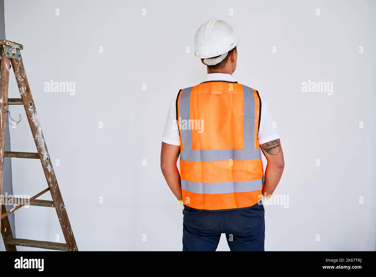The back of a construction worker as his faces blank wall with ladder ...