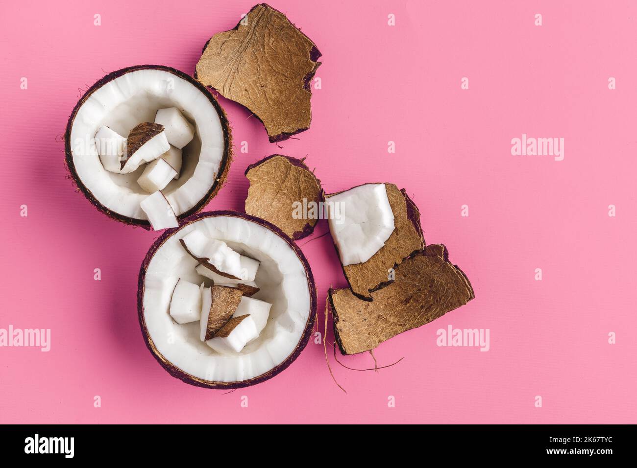 Broken coconut pieces on bright pink background, top view, copy space ...