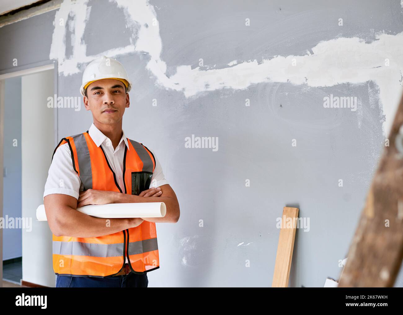 A serious construction worker stands with plans under his arm at home ...