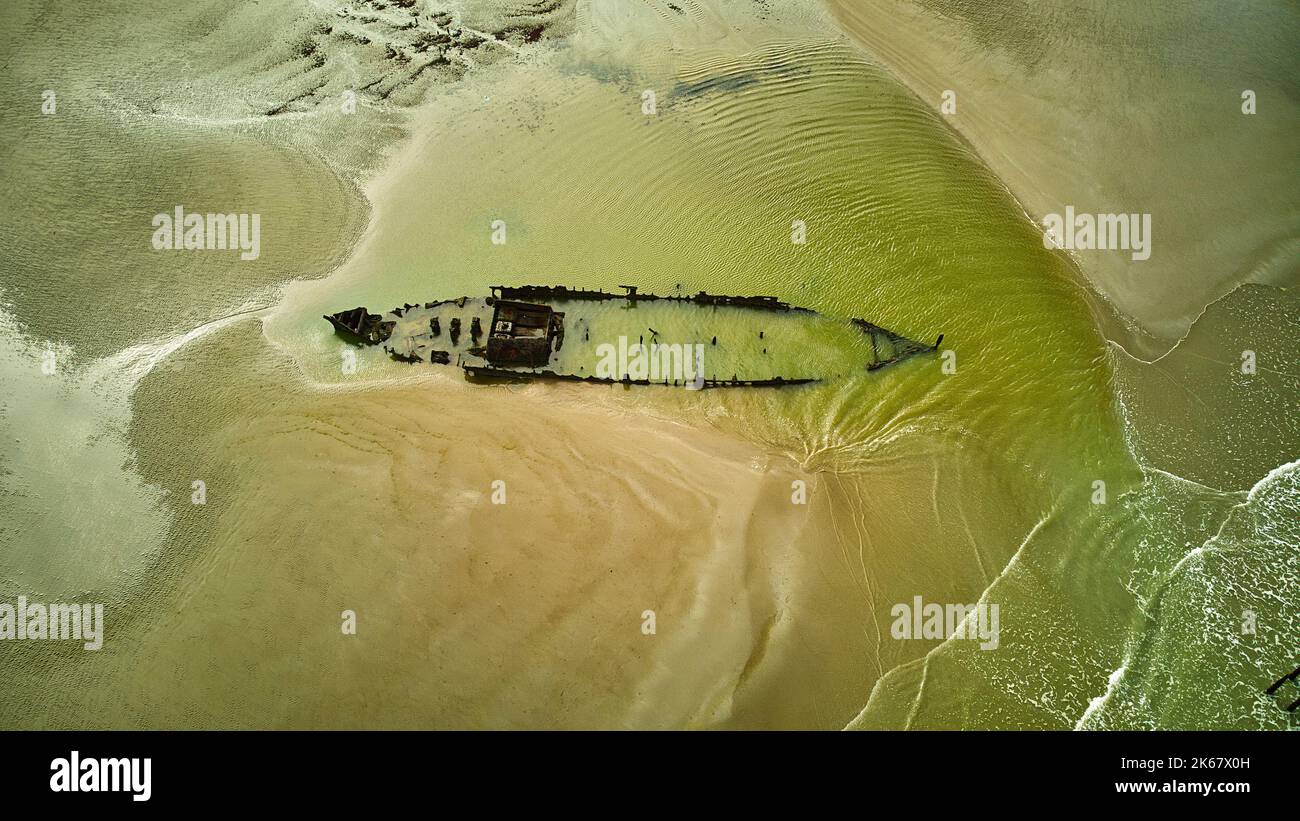 An aerial view of shipwreck in the shallow green sea water by the sandy ...