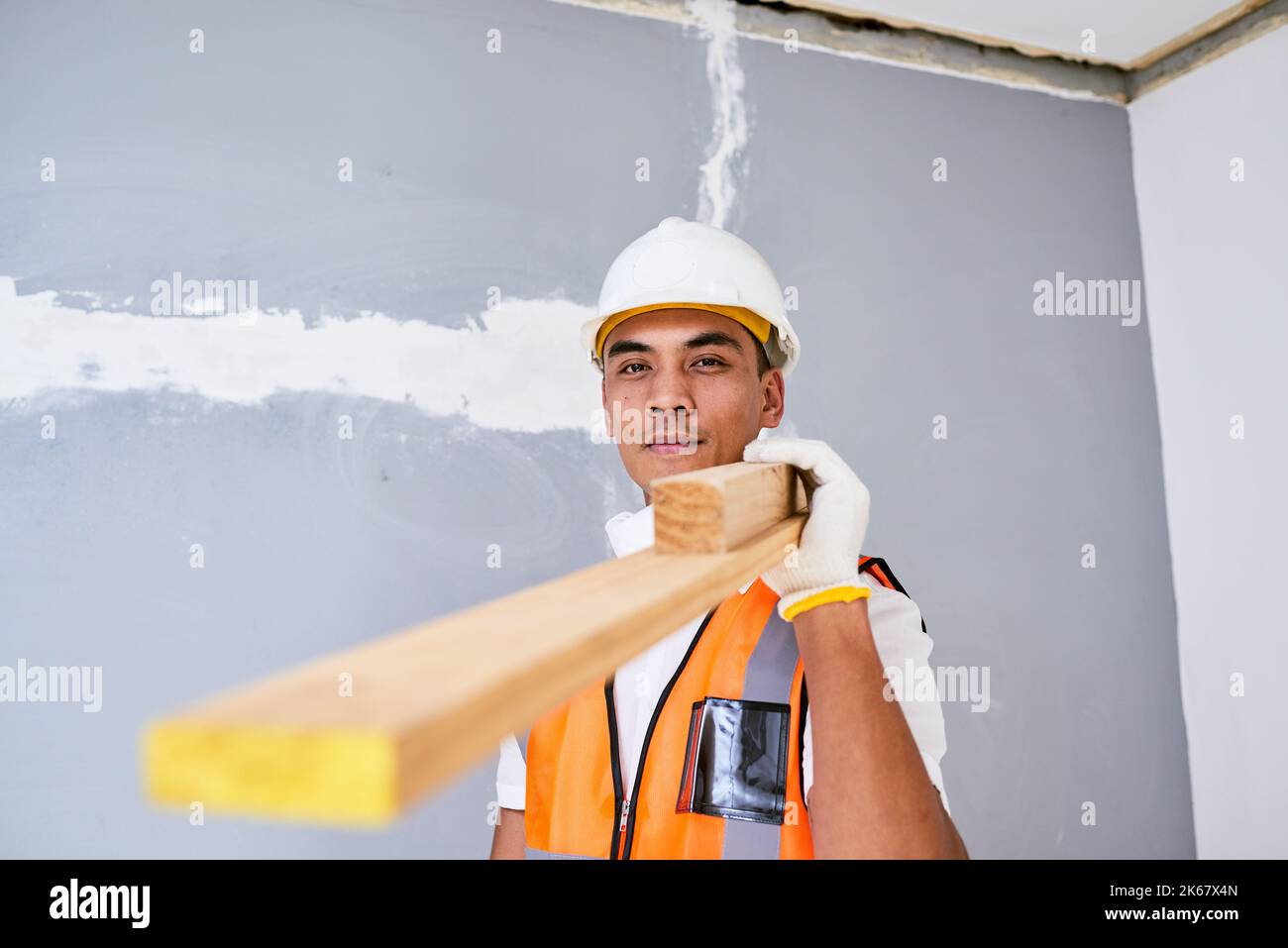 A young Filipino construction worker carries wooden planks on shoulder ...