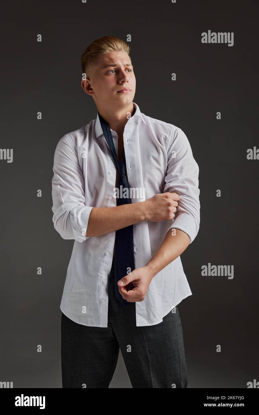 Portrait of young handsome man posing in white shirt isolated over dark ...