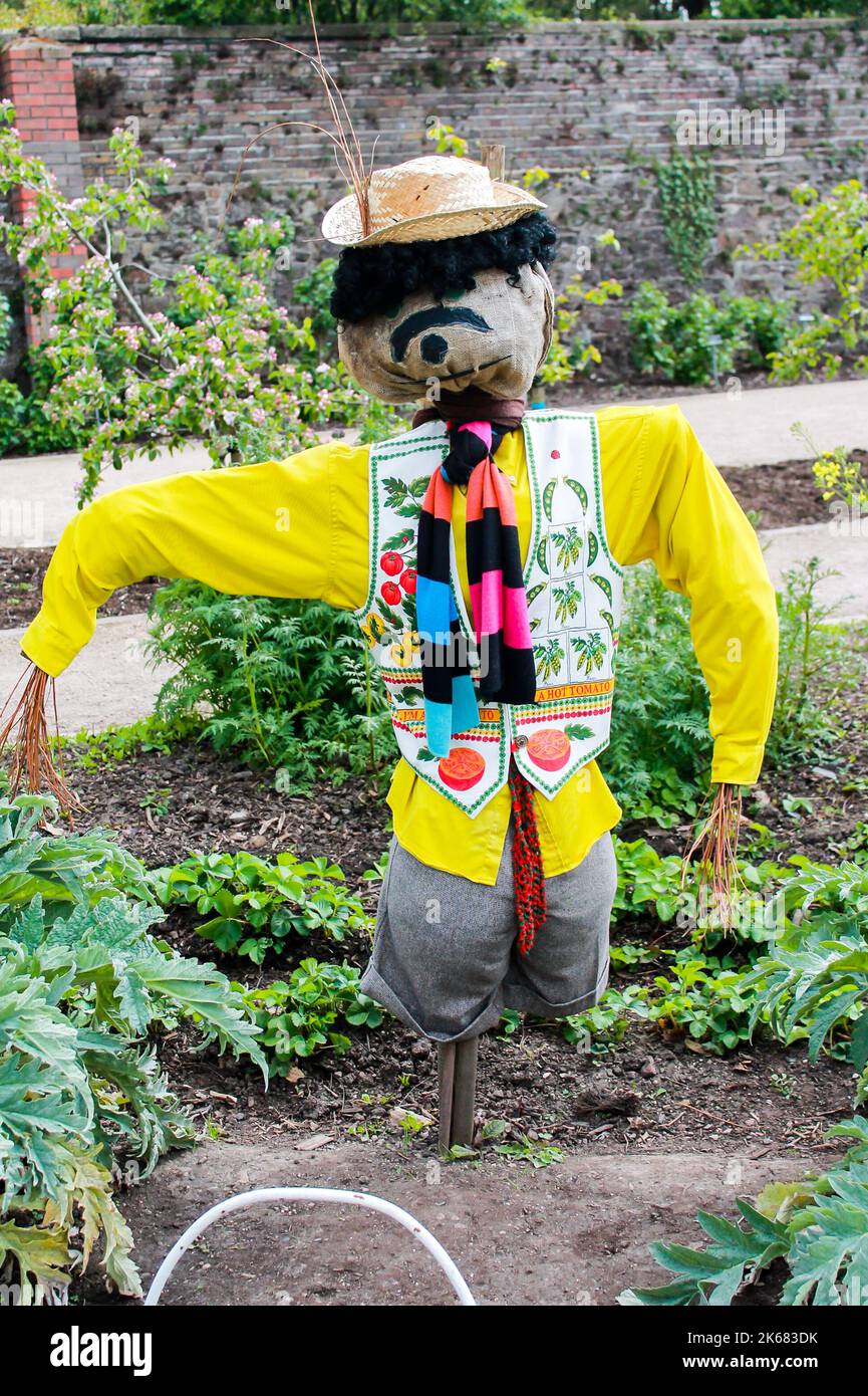 A vertical shot of a colorful scarecrow with plants and a brickwall in ...
