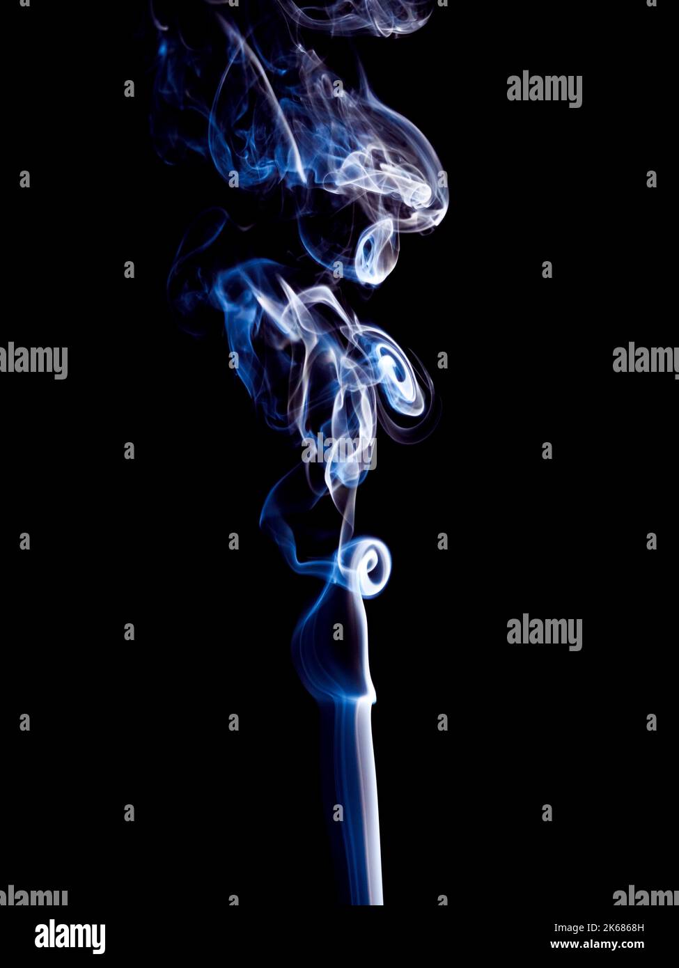A spectacular stream of blue and white smoke curls and rises on a black ...