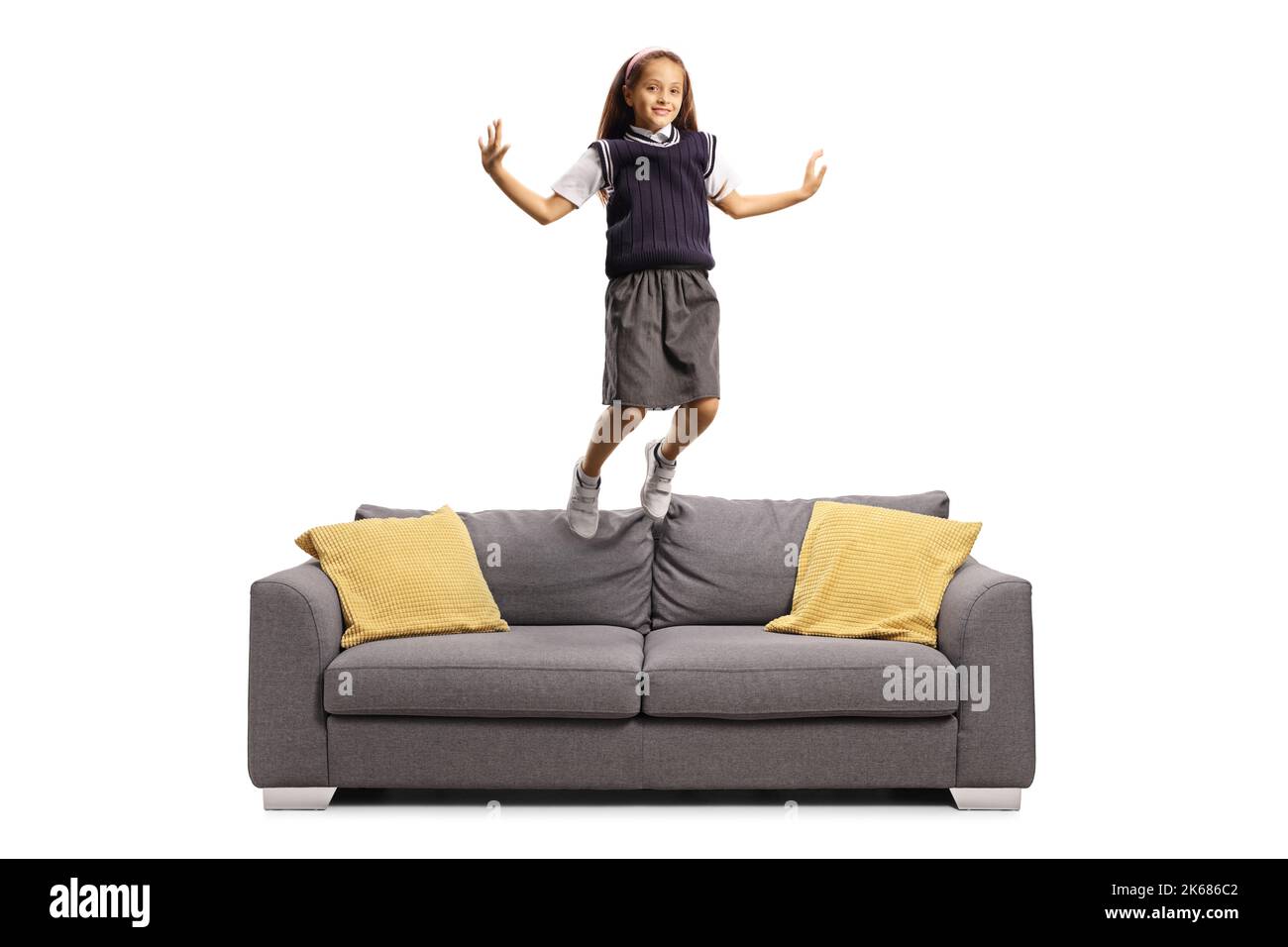 Schoolgirl in a uniform jumping on sofa isolated on white background ...