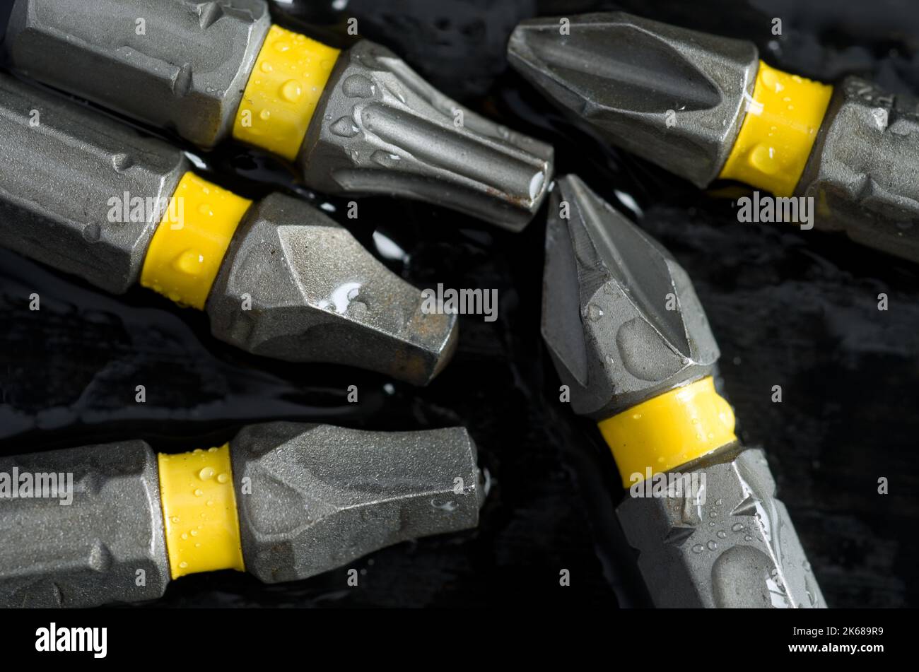 Macro of Multiple Screwdriver Drill Bits with Yellow Band on Wet Dark ...