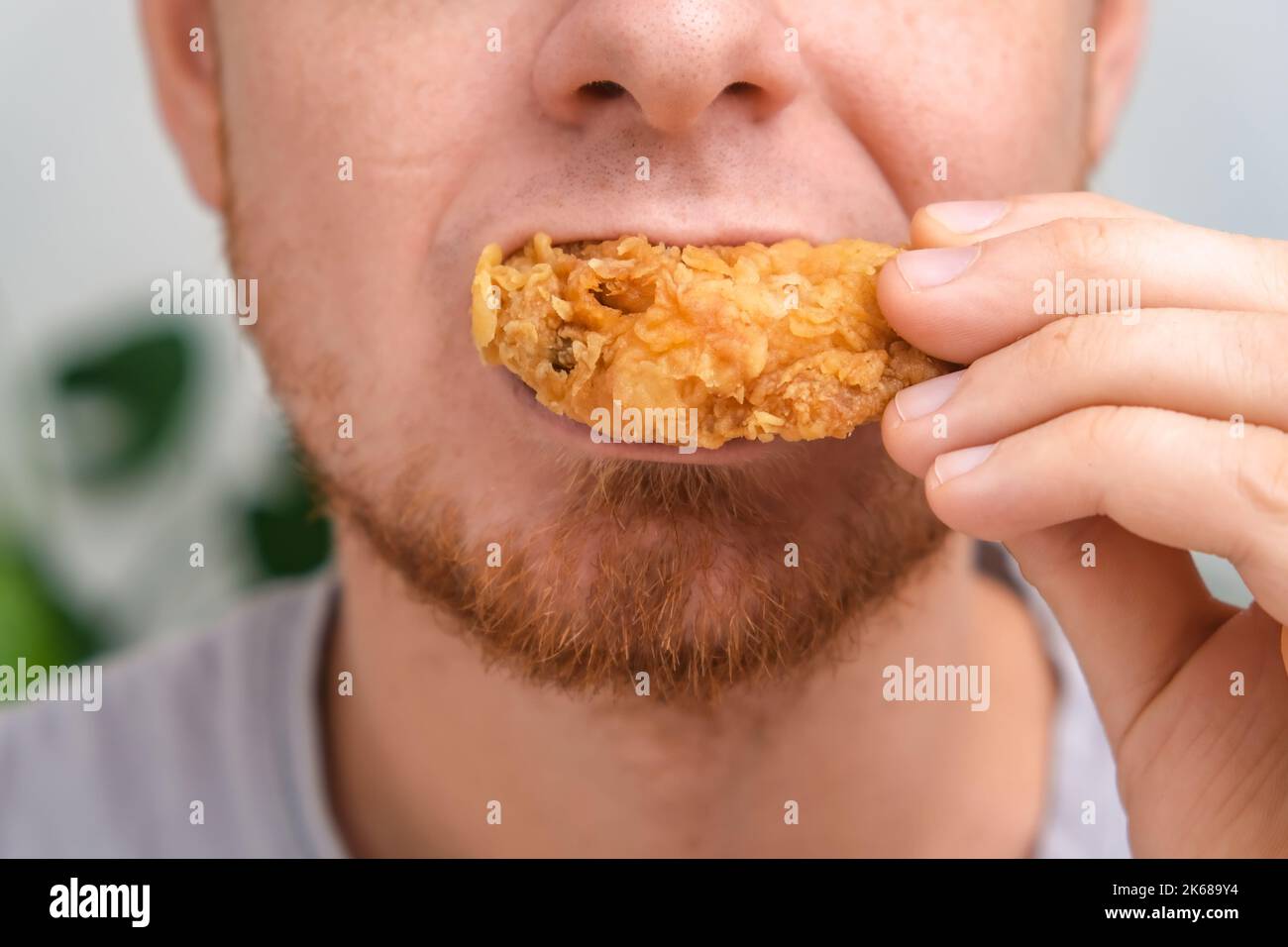 A man bites and chews a fried chicken wing in breadcrumbs. A man eats ...