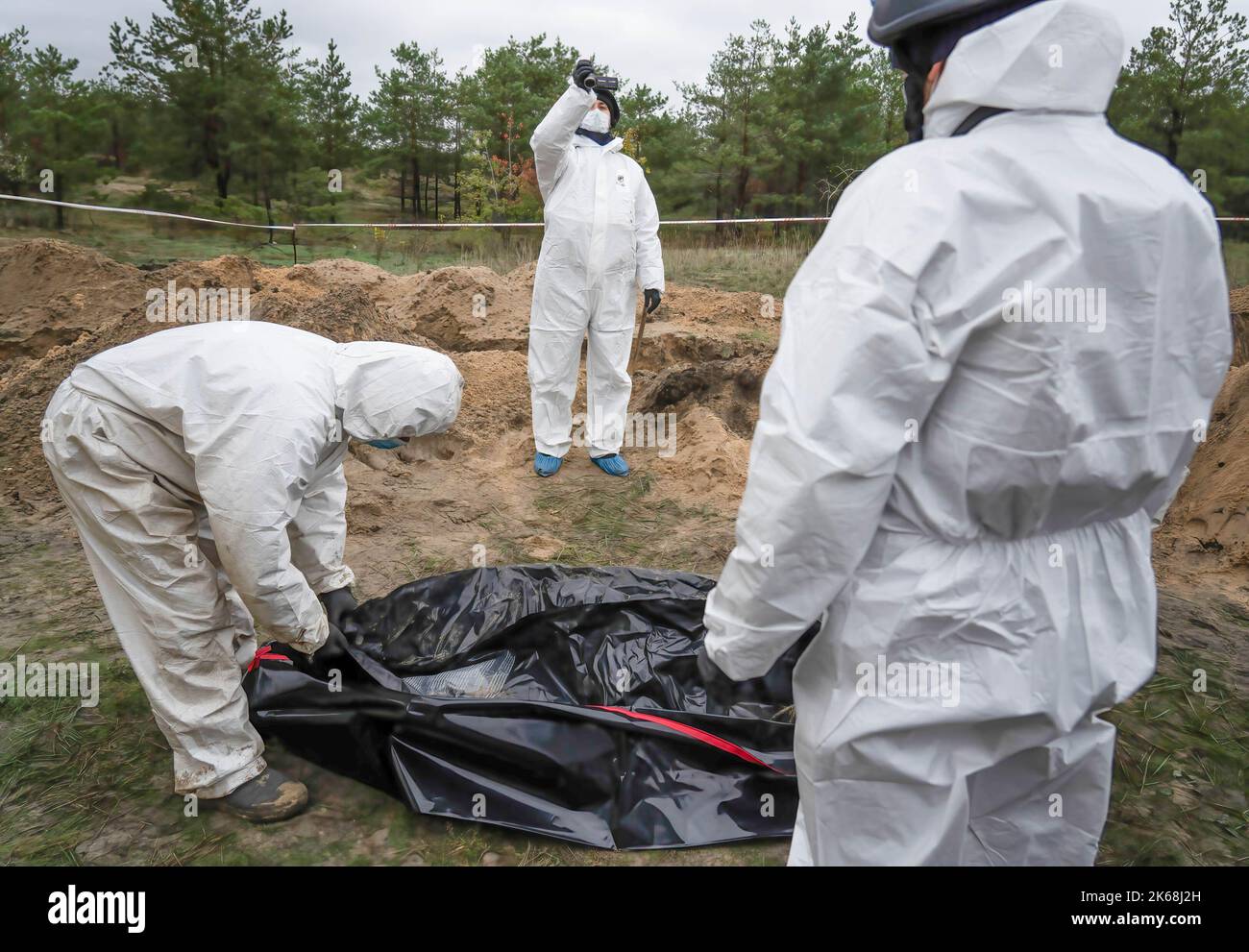 Investigators are seen zipping a body bag carrying an exhumed body in ...