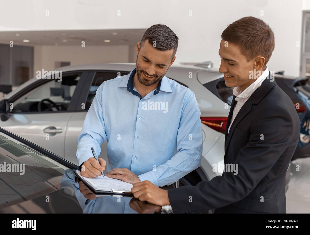 Young male consultant and buyer signing contract for new car in auto ...