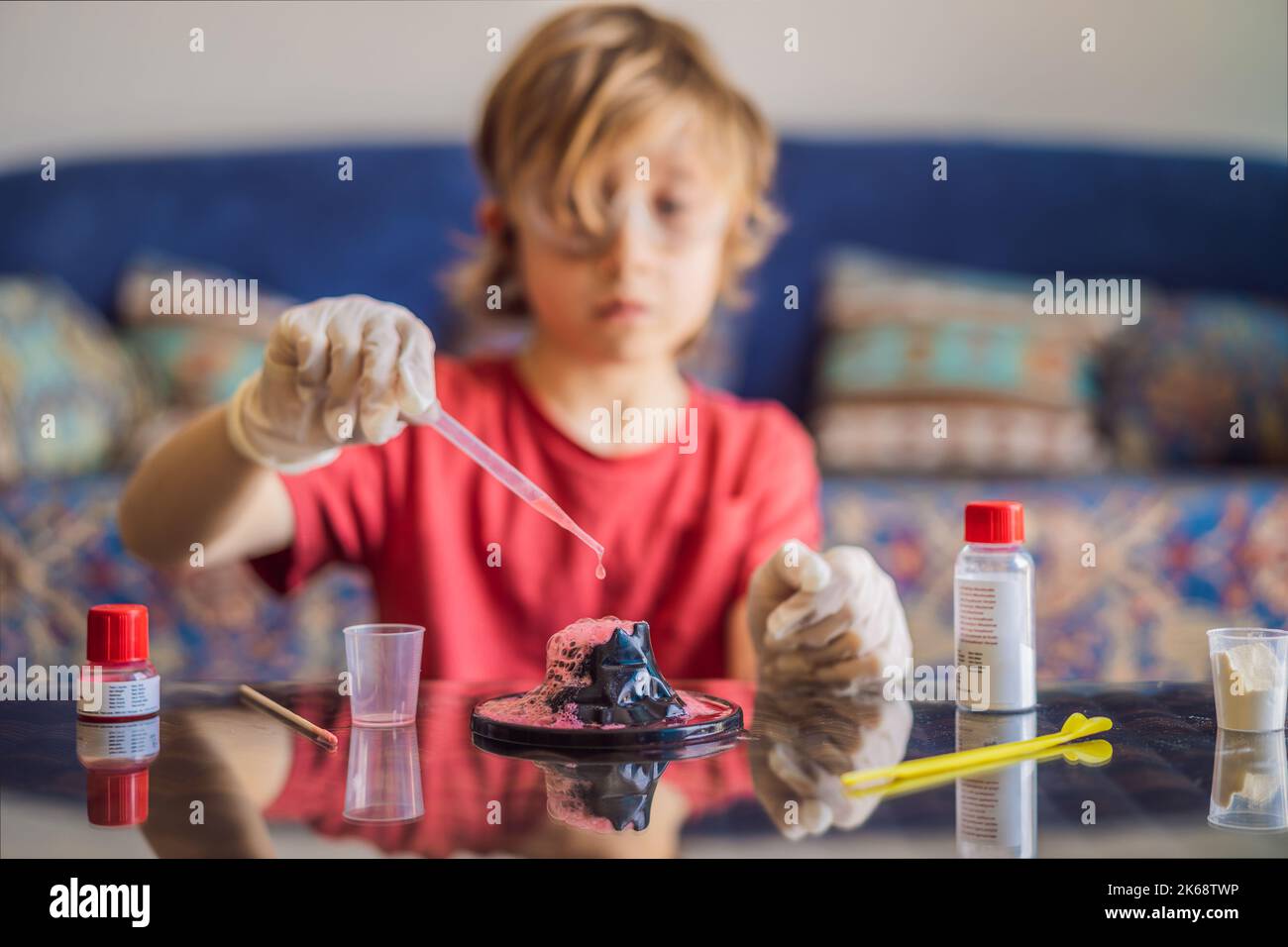 Kid boy doing chemical experiment at home. Child with protective glasses study using pipette ...