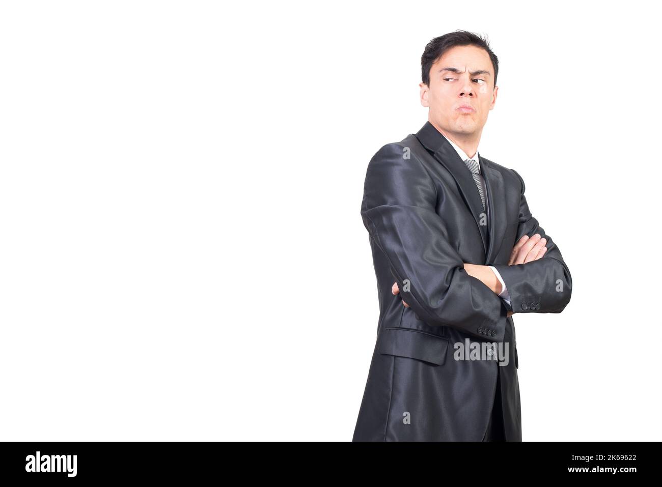 Distrustful young businessman looking away while standing with crossed ...