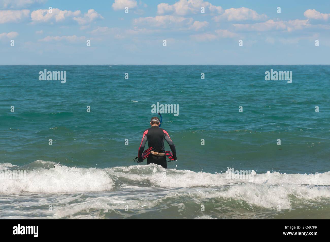 The diver carefully enters the sea through the coastal wave, holding ...