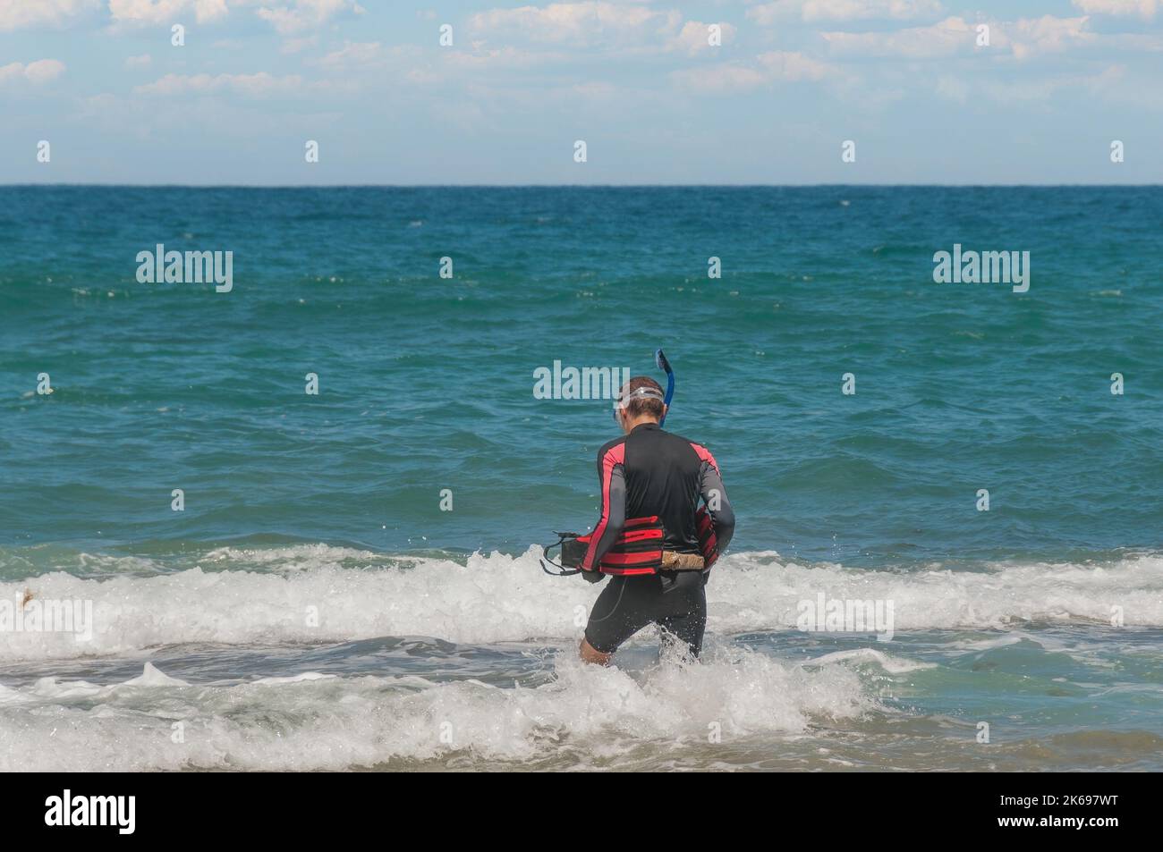The diver carefully enters the sea through the coastal wave, holding ...