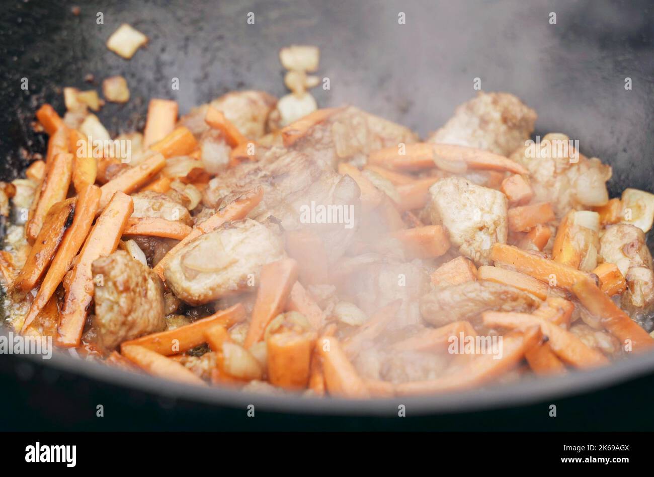 Close-up of a slotted spoon stirring meat, carrots and onions. Roasted ...