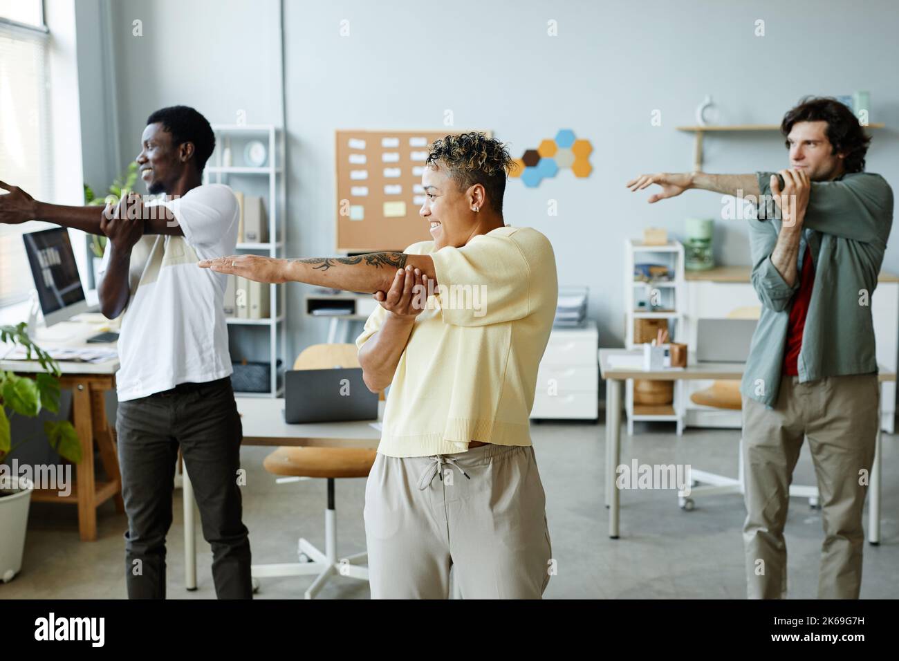 Diverse group of smiling young people doing stretching exercise during ...