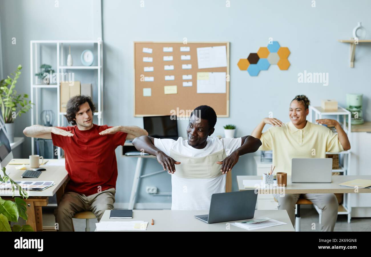 Diverse group of smiling young people stretching muscles as fun warm up ...