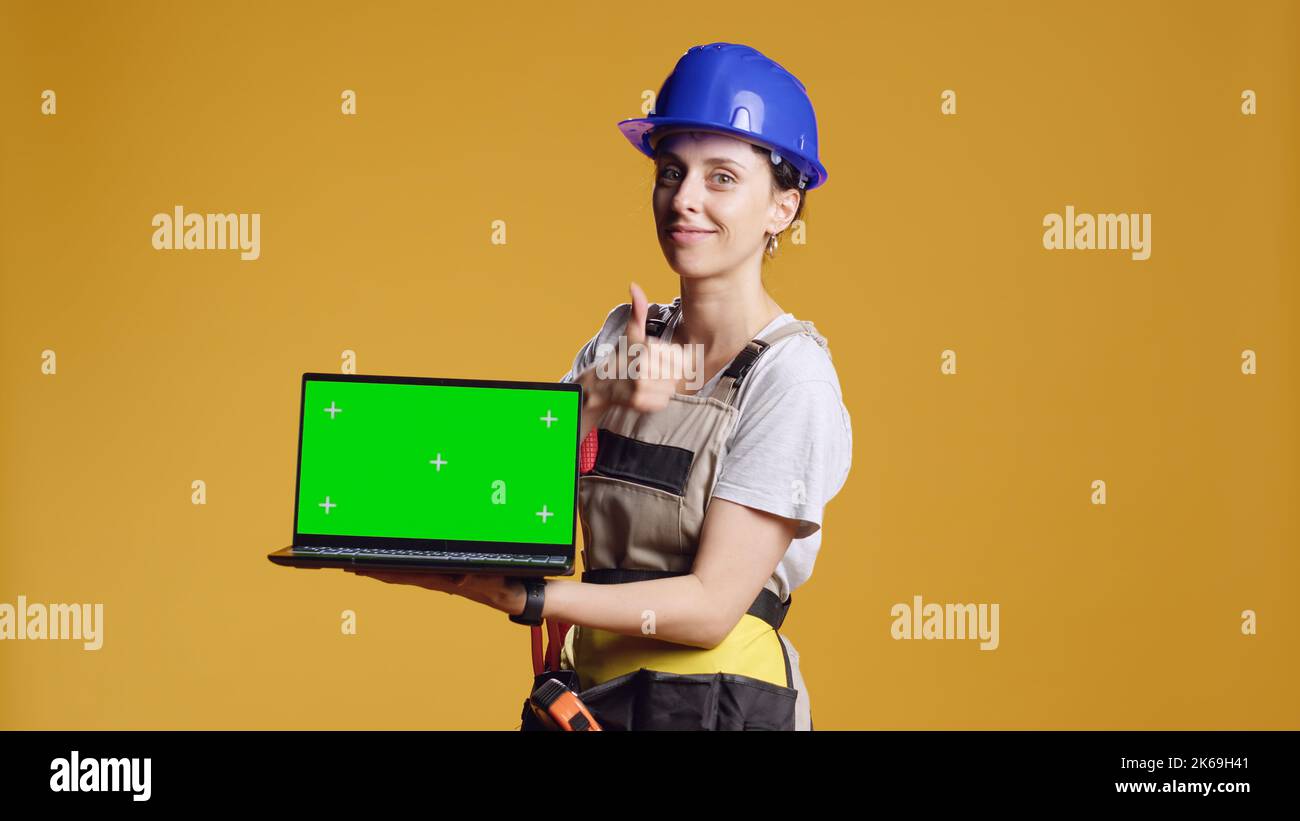 Female construction worker holding laptop with greenscreen in studio ...