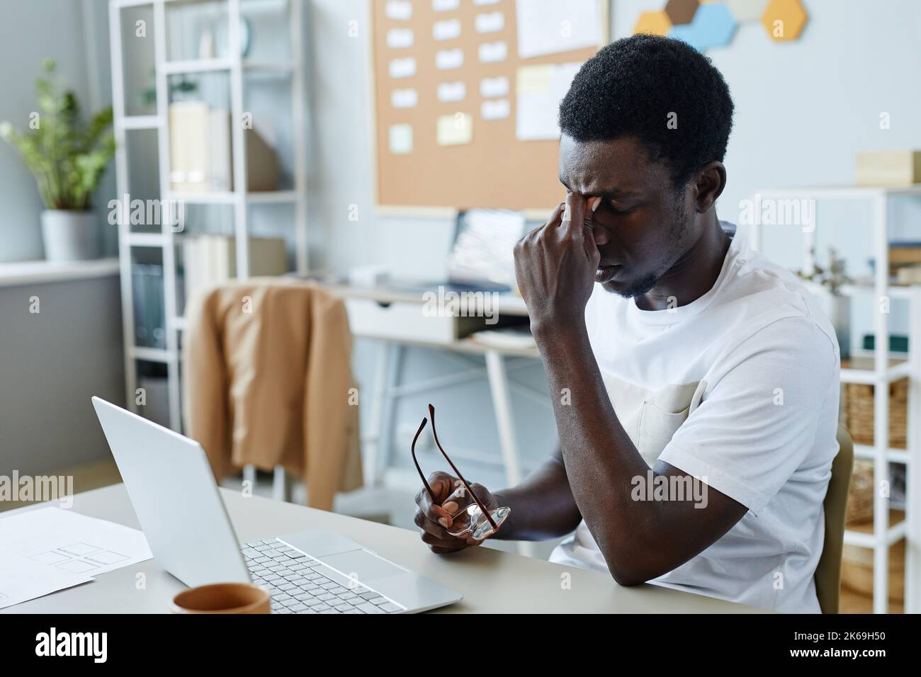 Portrait of frustrated black man taking off glasses at workplace and ...