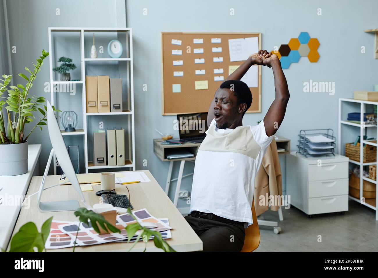 Portrait of exhausted young man stretching and yawning at office ...