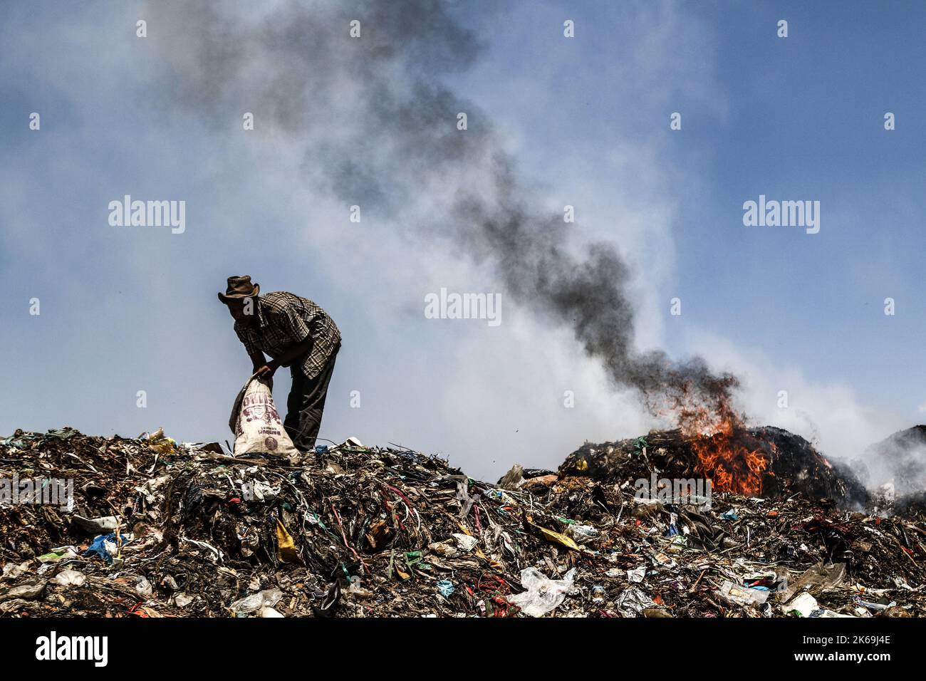 A scavenger retrieves materials for recycling beside burning rubbish at ...