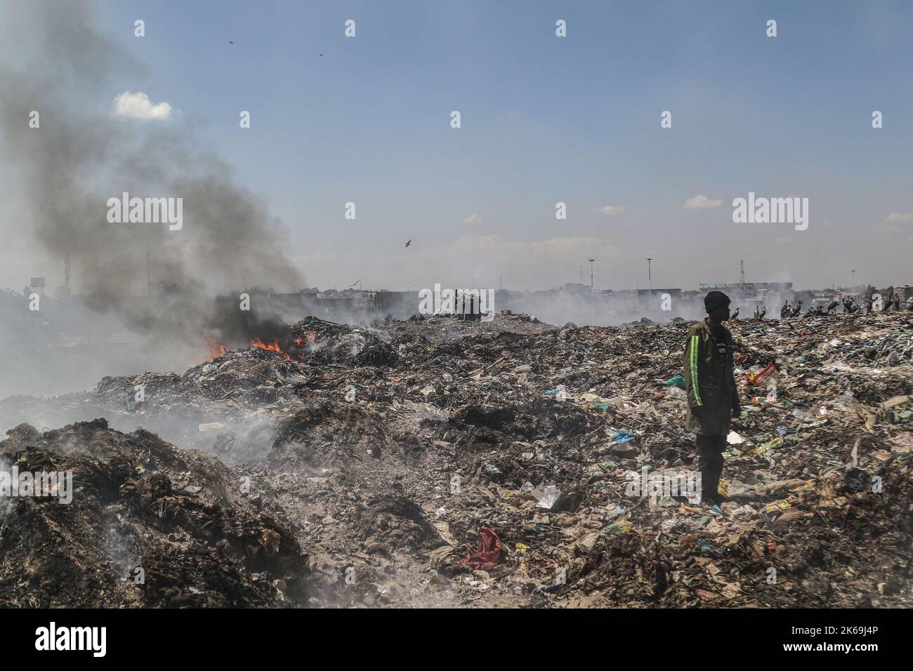 A scavenger stands near burning rubbish at Dandora Dumping Site. There ...