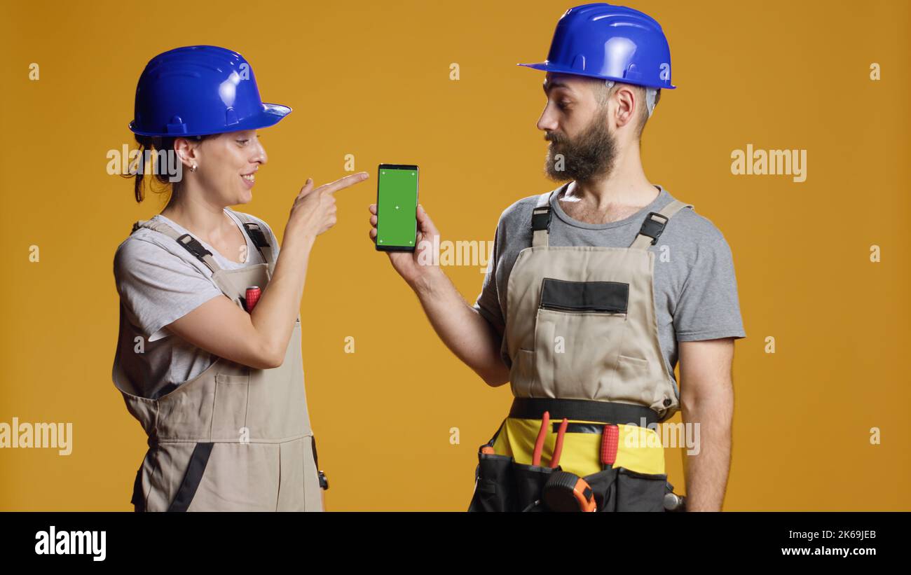 Portrait of building contractors pointing at smartphone with ...