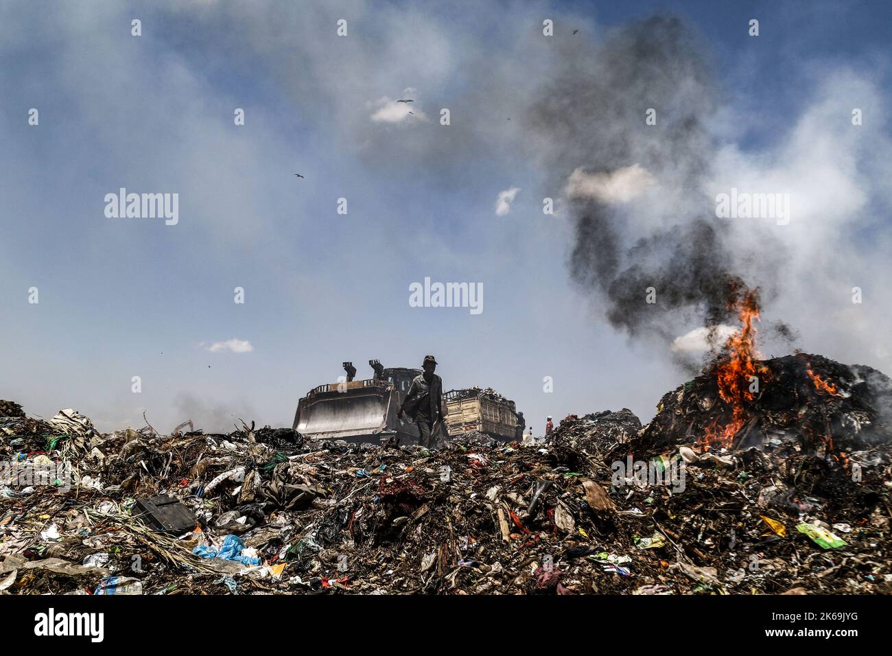 A scavenger retrieves materials for recycling beside burning rubbish at ...