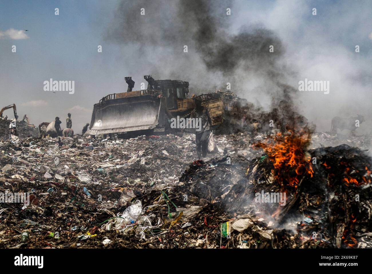 A scavenger retrieves materials for recycling beside burning rubbish at ...