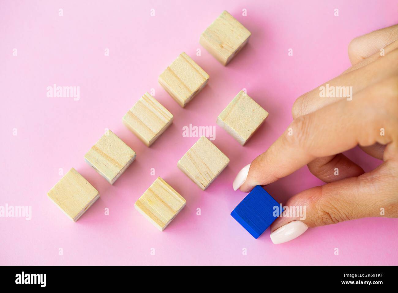 Wooden blocks with a human hand placing one cube at the top on pink ...