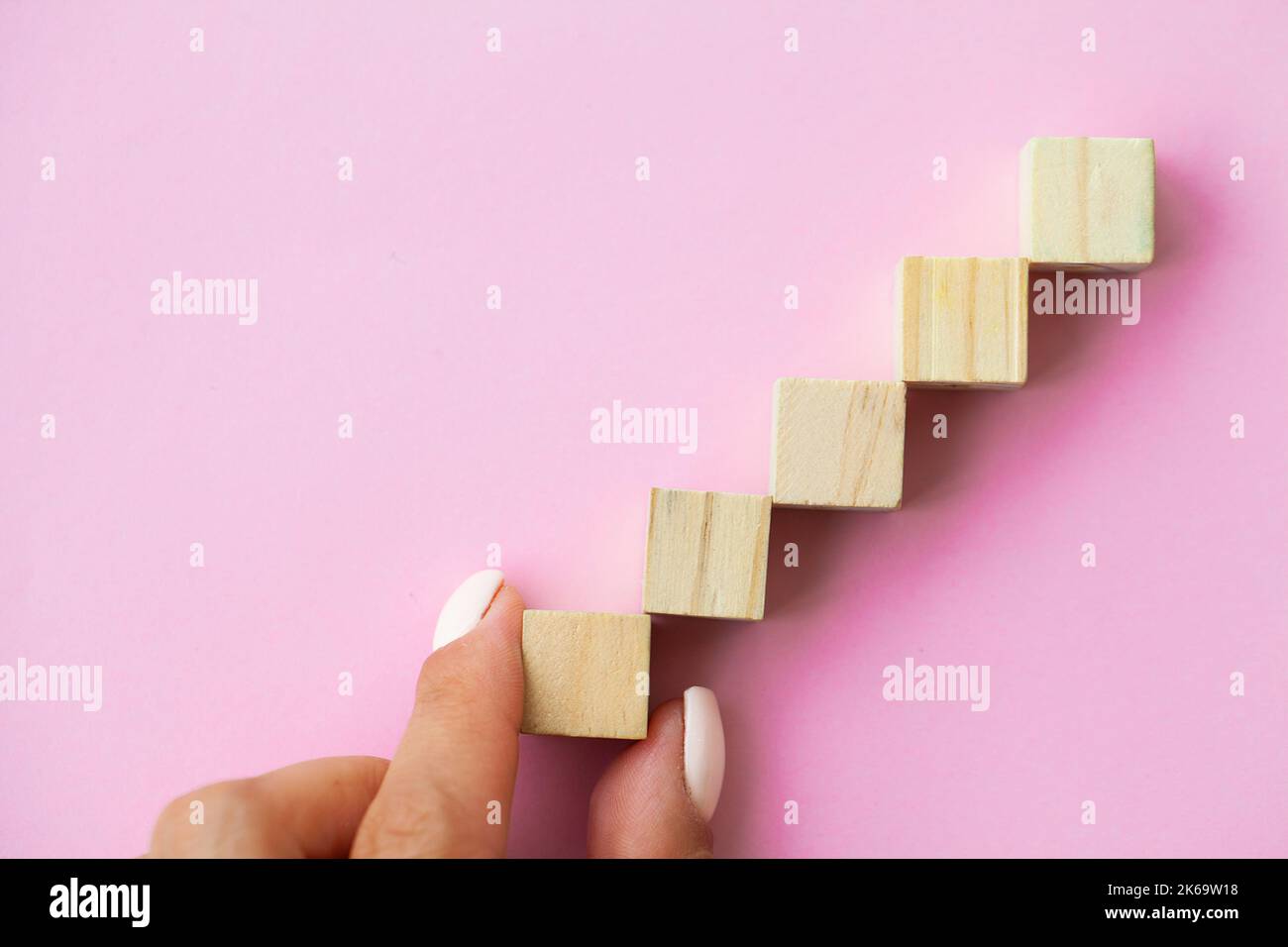 Wooden blocks with a human hand placing one cube at the top on pink ...