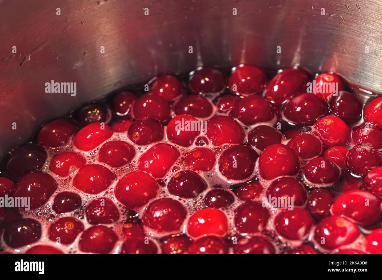 Cranberries cooking on a stovetop in a stainless steel pot making ...