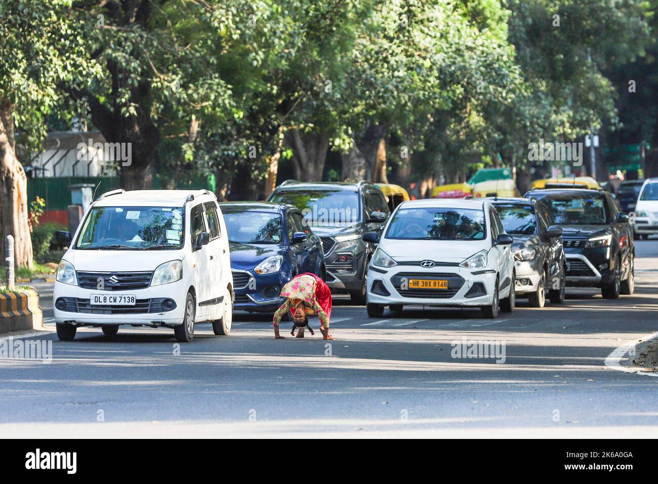 A poor girl child performs acrobatics in front of vehicles at a traffic ...