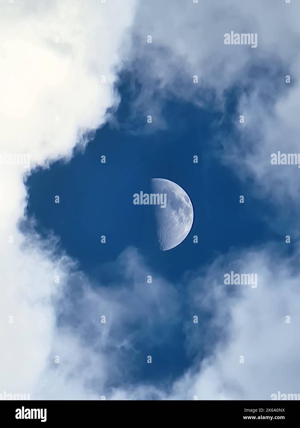 A vertical closeup of a half-moon in a daytime sky with clouds Stock ...