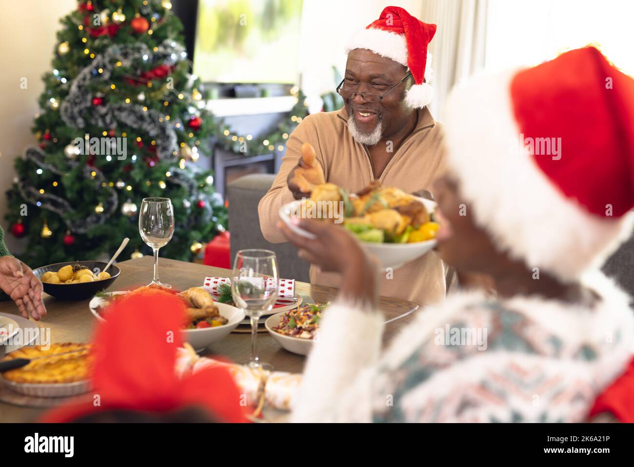 Happy african american family wearing santa hats, sitting at table and ...