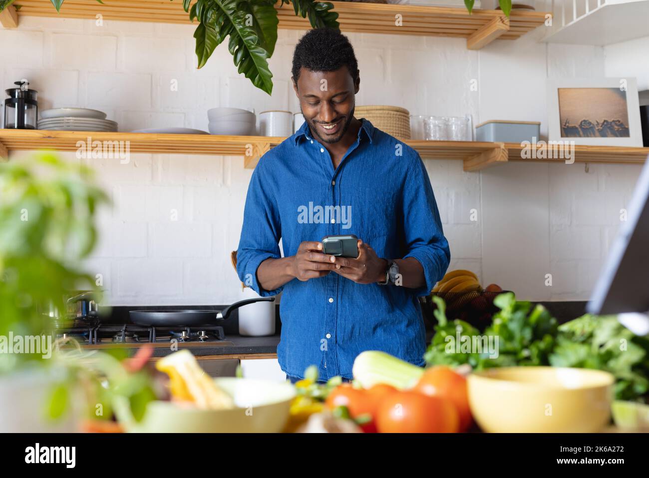 Happy african american man cooking dinner in kitchen, using smartphone ...