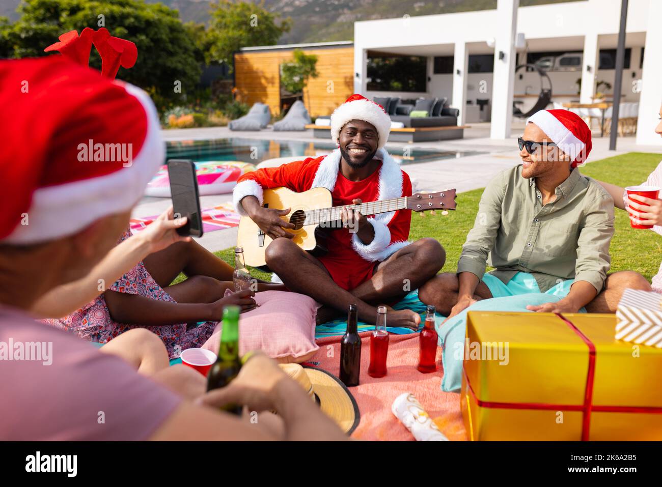 Happy diverse friends with santa hats having picnic in garden at ...
