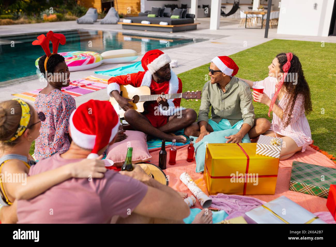 Happy diverse friends with santa hats having picnic in garden at ...