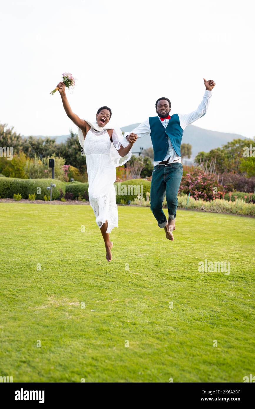 Portrait of happy african american couple holding hands and jumping ...