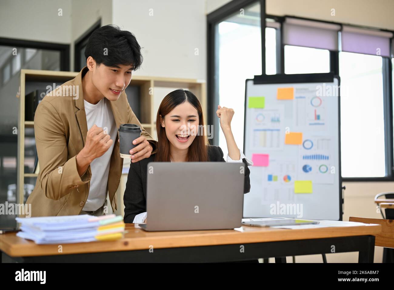 Happy and overjoyed Asian business colleagues triumph, looking at ...