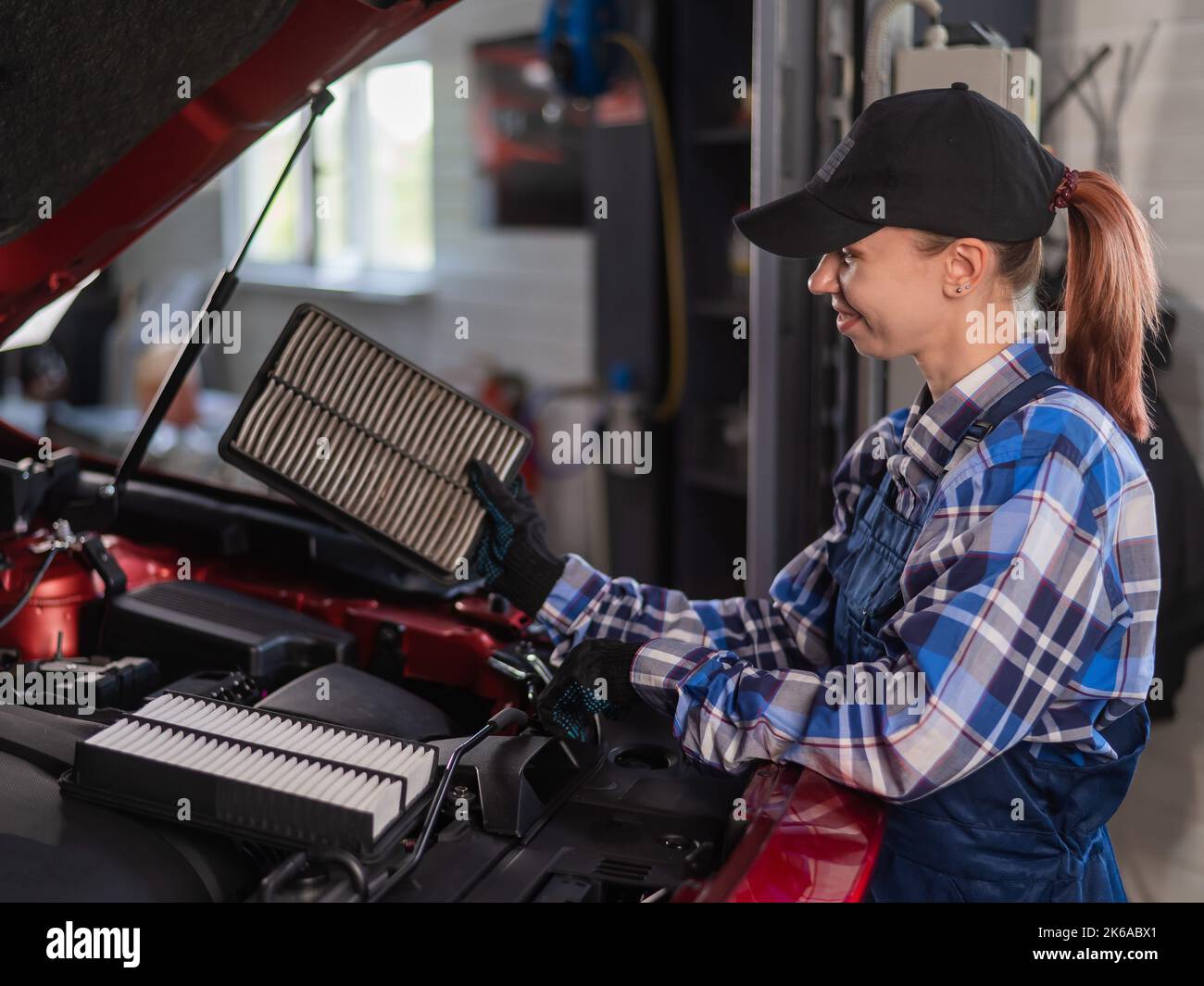 Caucasian female auto mechanic changes the engine air filter in the car ...