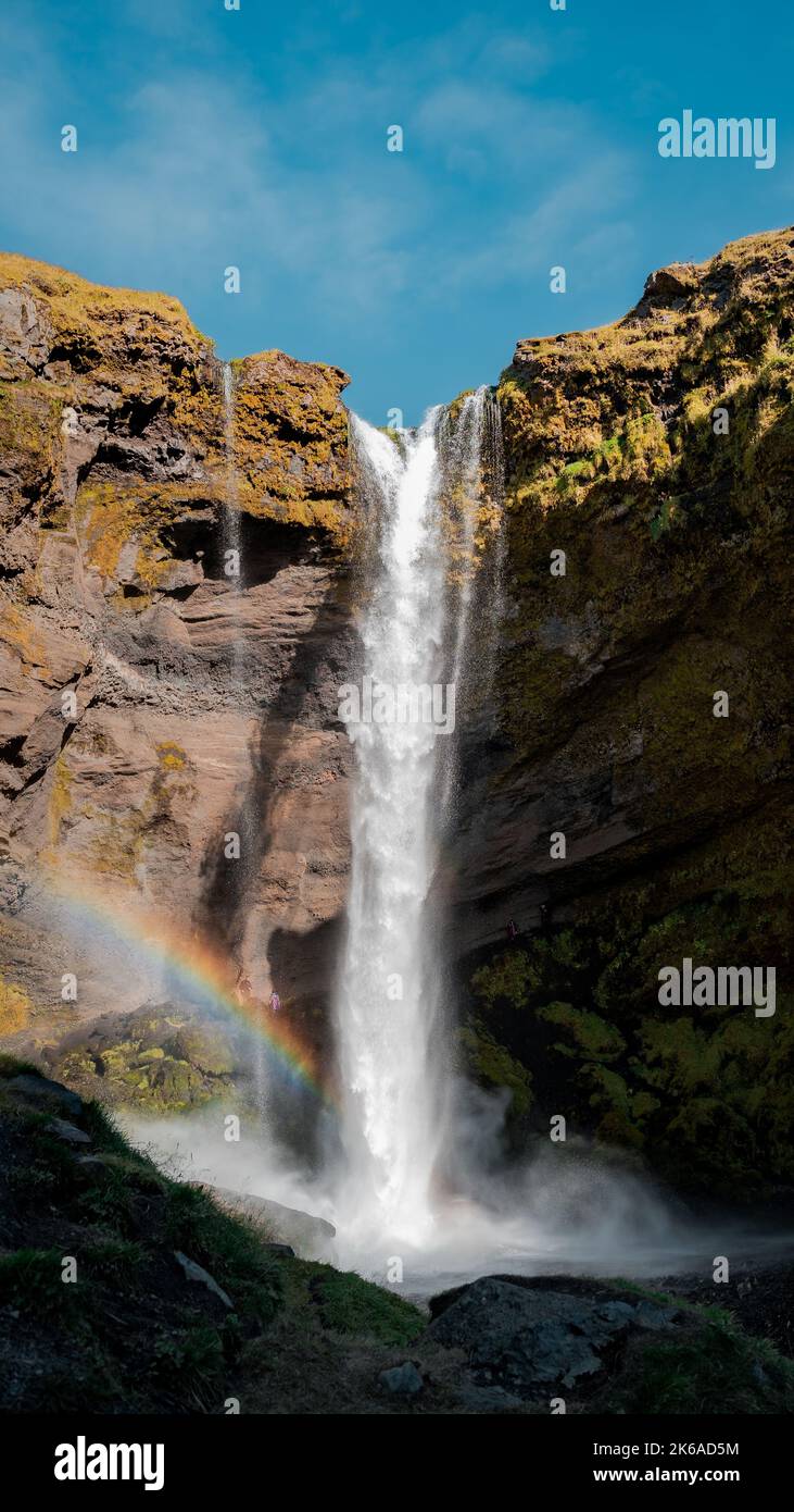 A vertical shot of a waterfall flowing from a mossy cliff with a ...