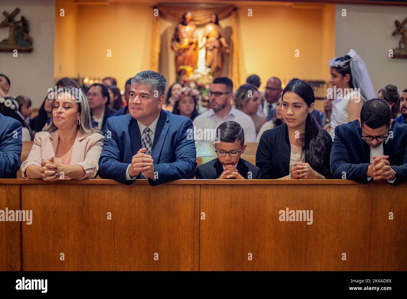 Adults and children of different ages fill the first pew of a Catholic ...