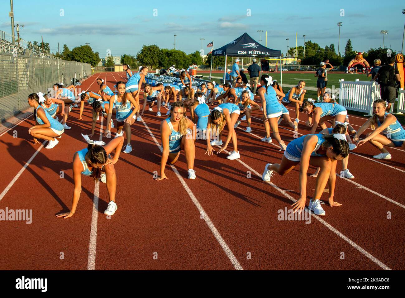 Blue-uniformed multiracial high school cheerleaders exercise to limber ...