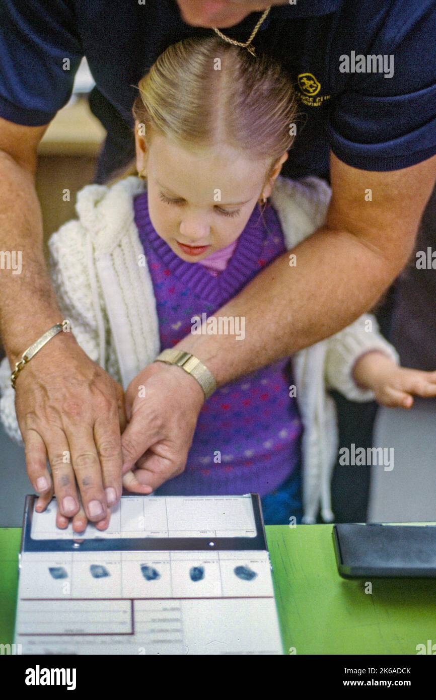 A father helps his young daughter give her fingerprints to be stored ...