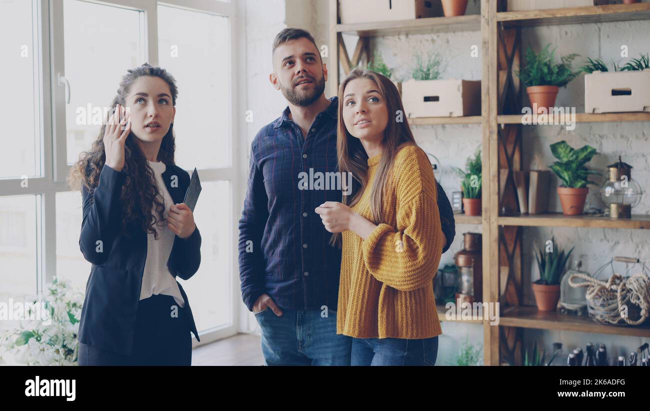 Confident realtor is describing advantages of new house to young couple ...