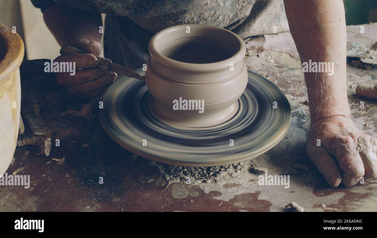 Close-up shot of male hands decorating ceramic pot with little knife on ...