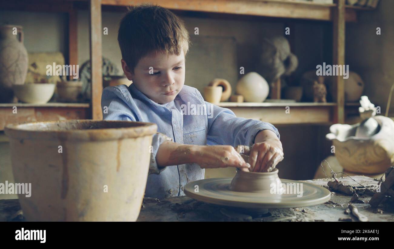Serious young boy student of pottery class is molding clay on spinning ...