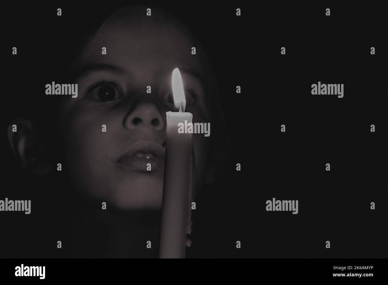 A little Ukrainian girl pray near a candle in the dark, a prayer to God ...