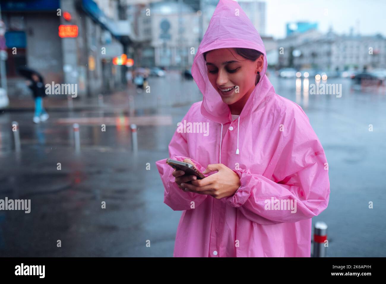 A young woman in a raincoat looking at the smartphone Stock Photo - Alamy